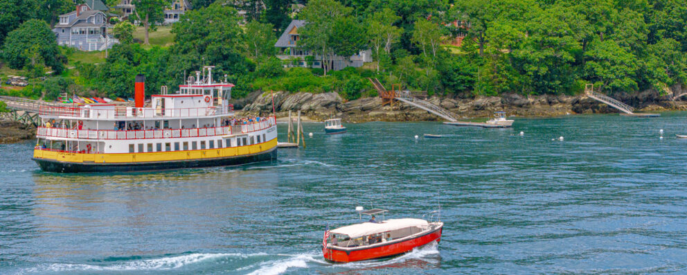 red boat sailing past rocky island and yellow ferry boat on blue water ...